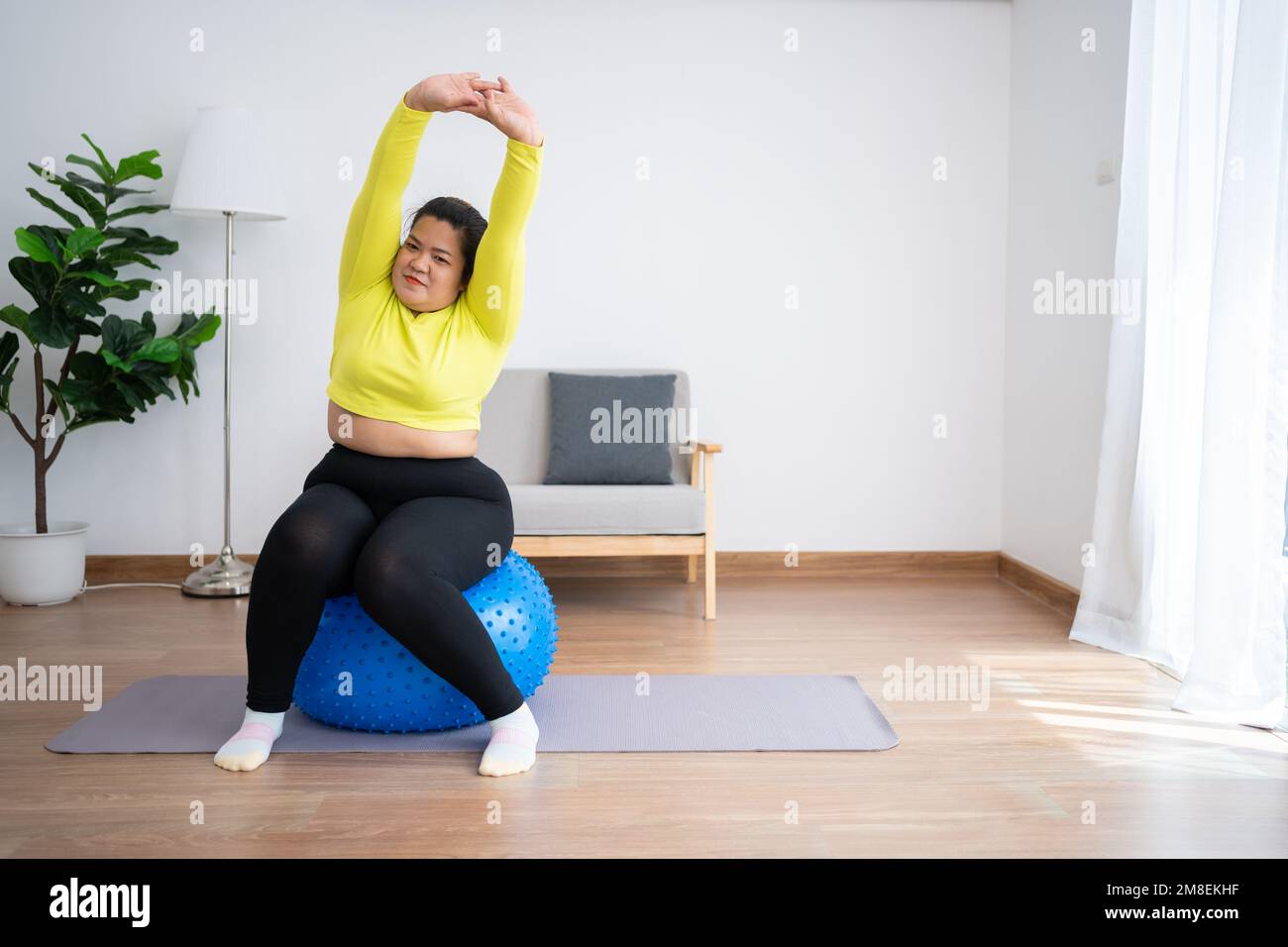 Portrait plus size woman doing exercise with fitness ball in home gym ...
