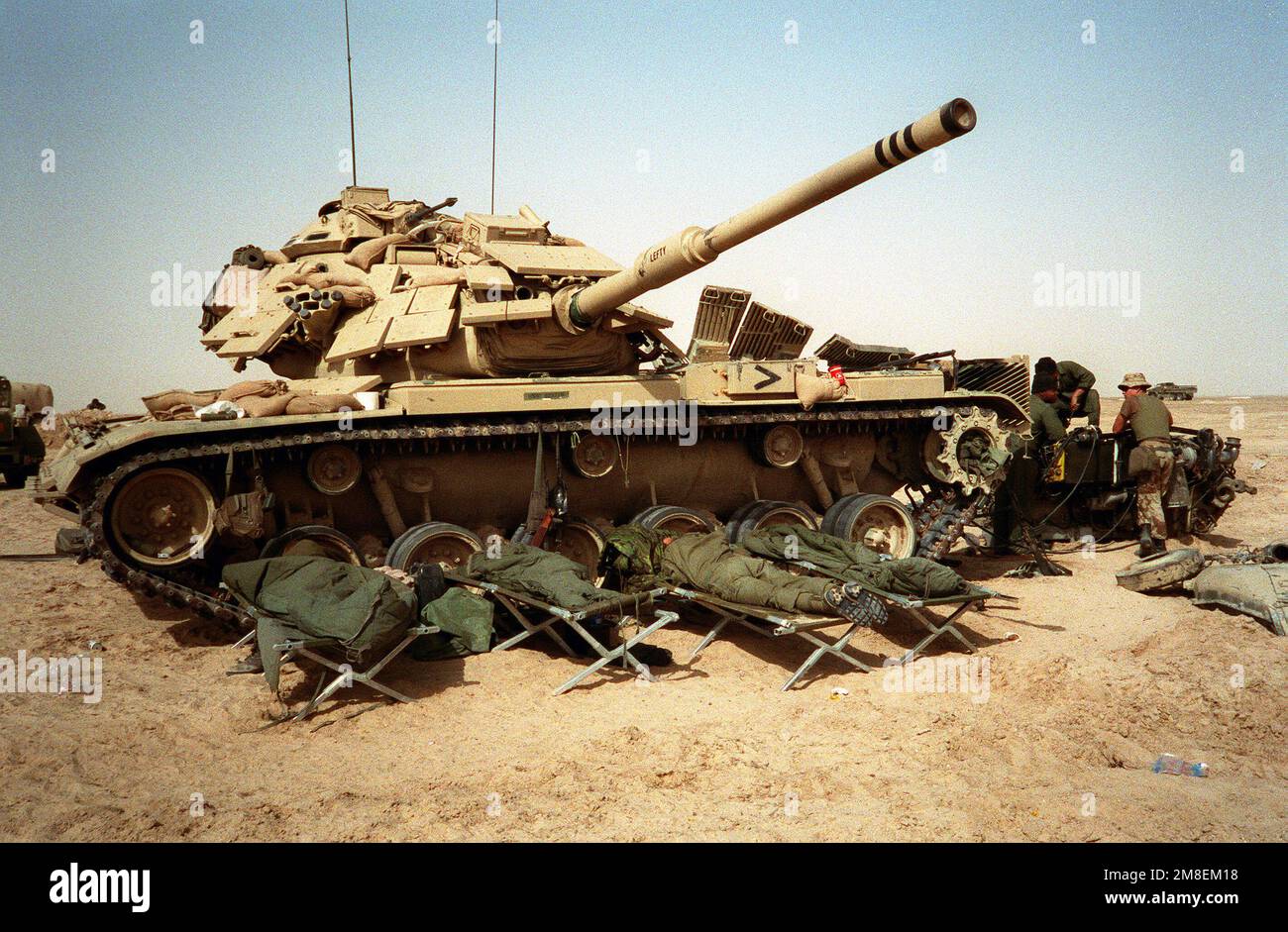 A Marine naps in his cot as other Marines work on the power pack from ...