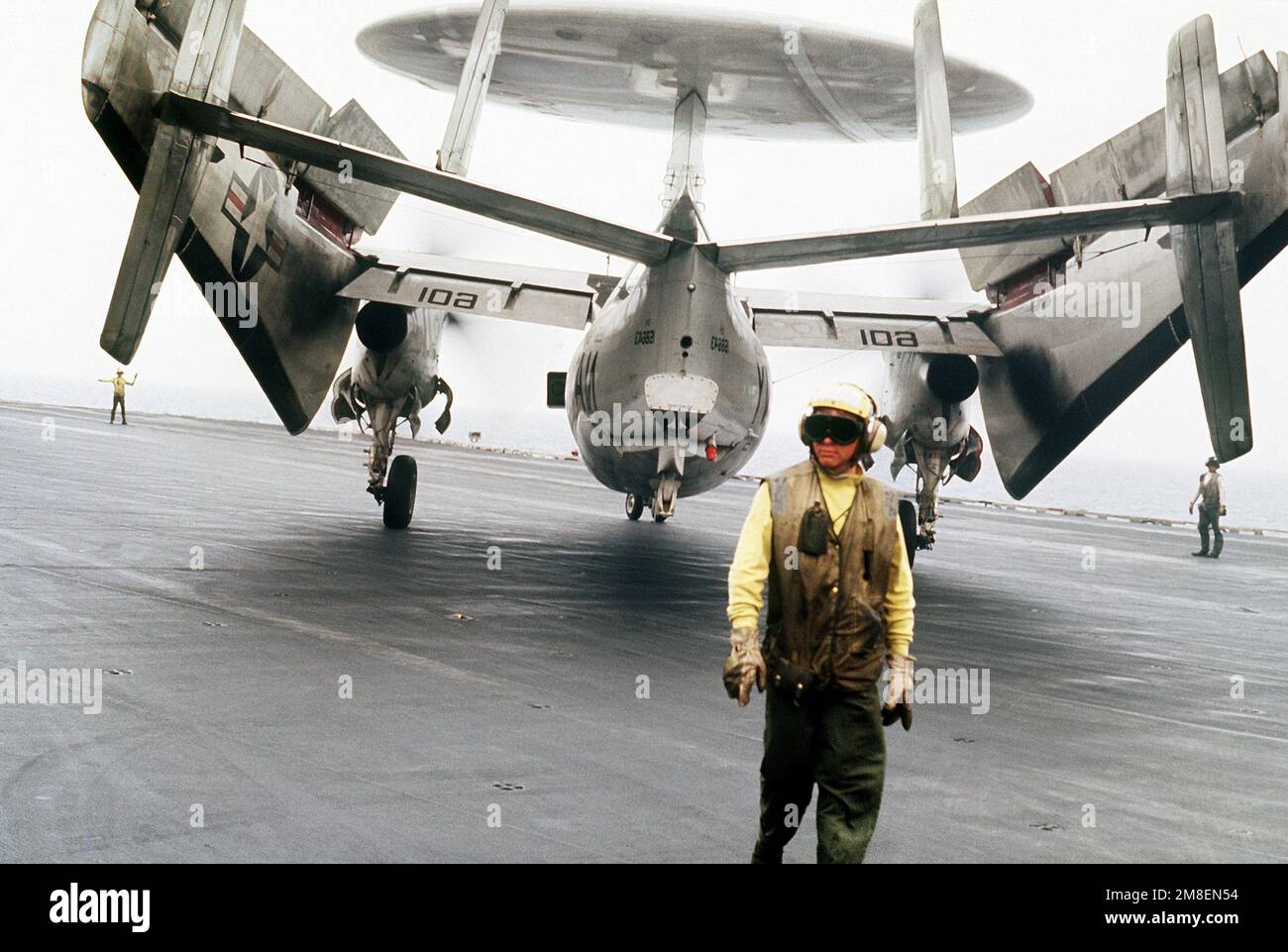A flight deck crew member stands behind an E-2C Hawkeye aboard the ...
