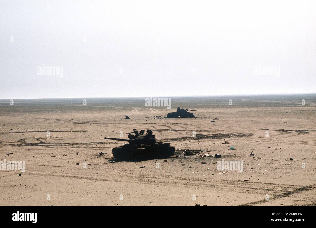 Two destroyed Iraqi T-55A main battle tanks lie in the sand beside a ...