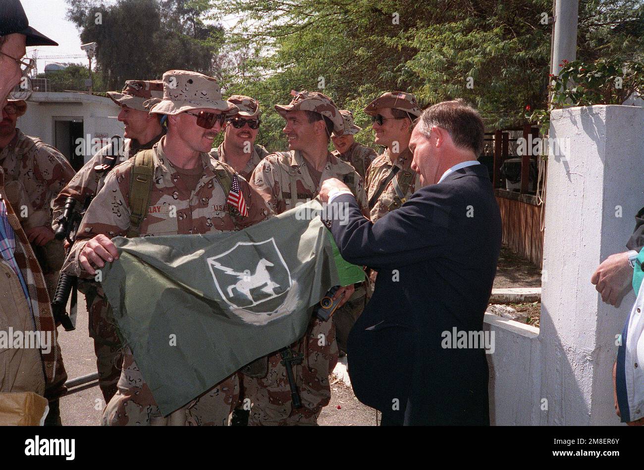 A U.S. Army soldier presents his unit's flag to Edward Gnehm, the U.S ...