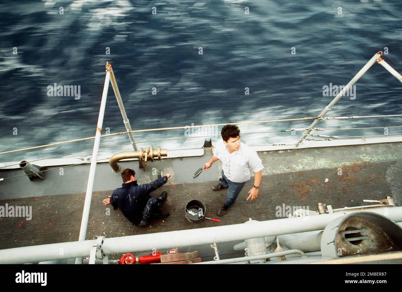 A pair of crewmen paint part of the deck of the guided missile ...