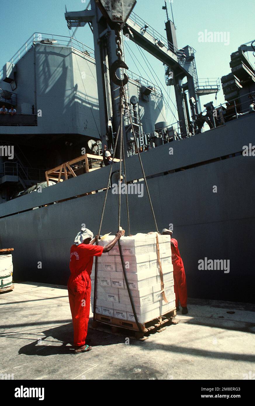 Dock workers steady a pallet of supplies as it is hoisted aboard the Military Sealift Command ...