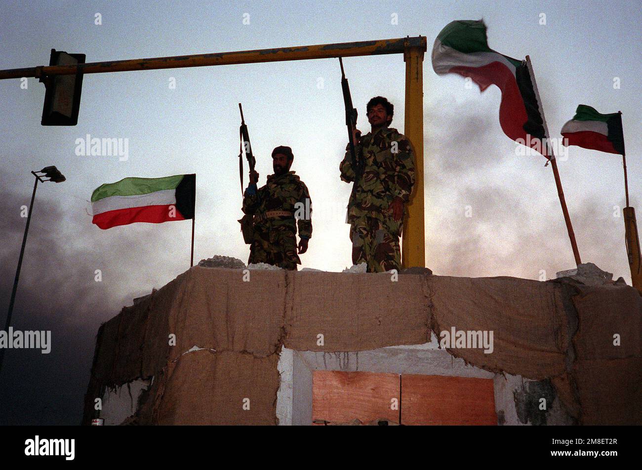 Kuwaiti guards armed with M-16 rifles stand beside their nation's flag ...