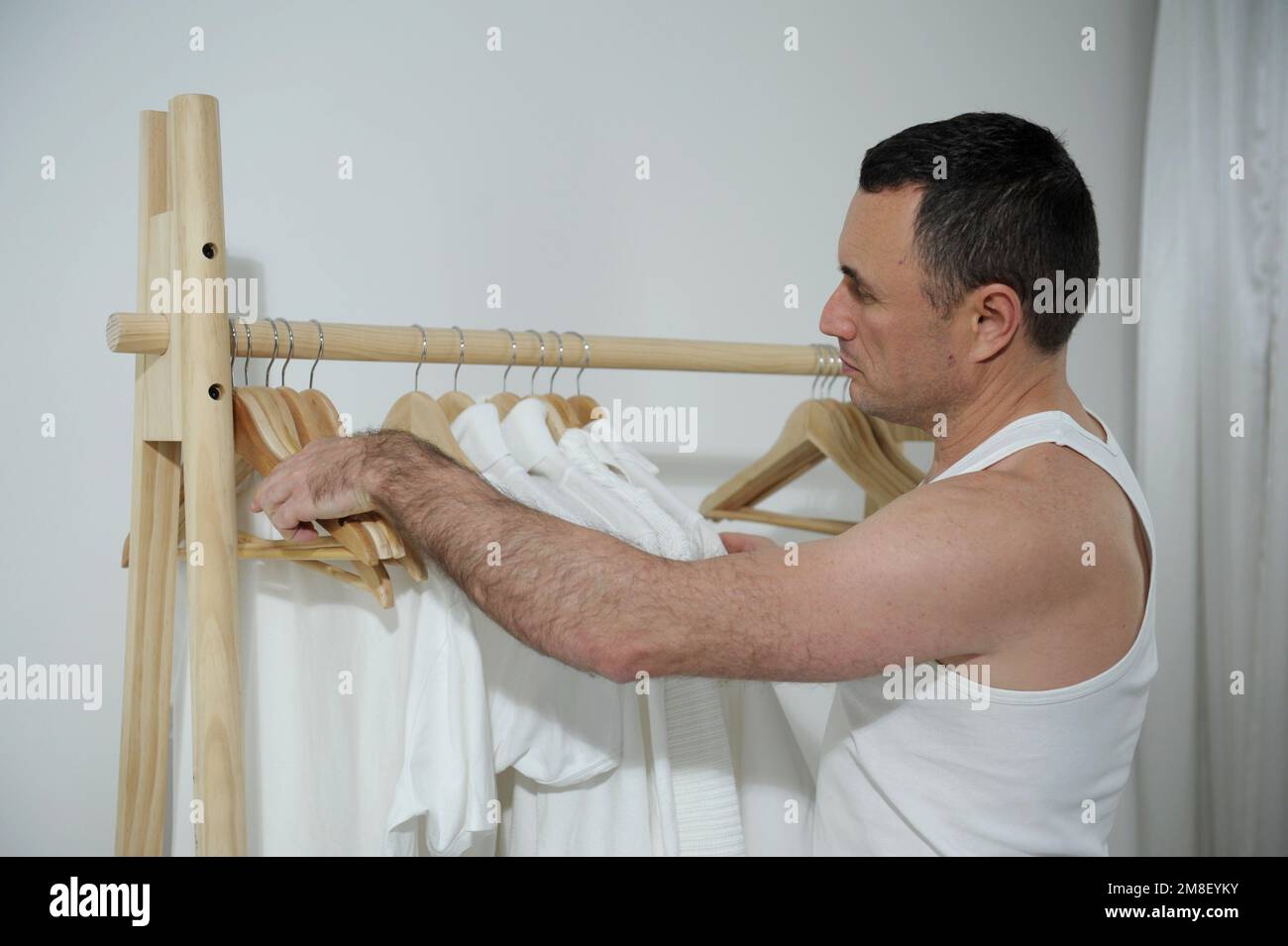 handsome adult man with hairy arms in white t-shirt stands near wooden ...
