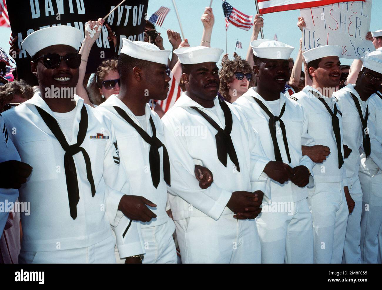 A line of sailors holds back the crowd gathered to greet the guided ...