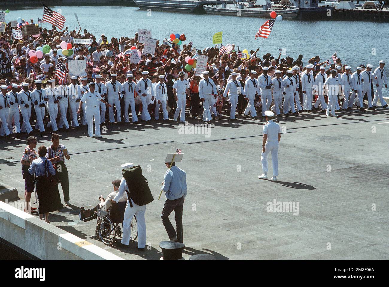 A line of sailors holds back the crowd gathered to greet the guided ...