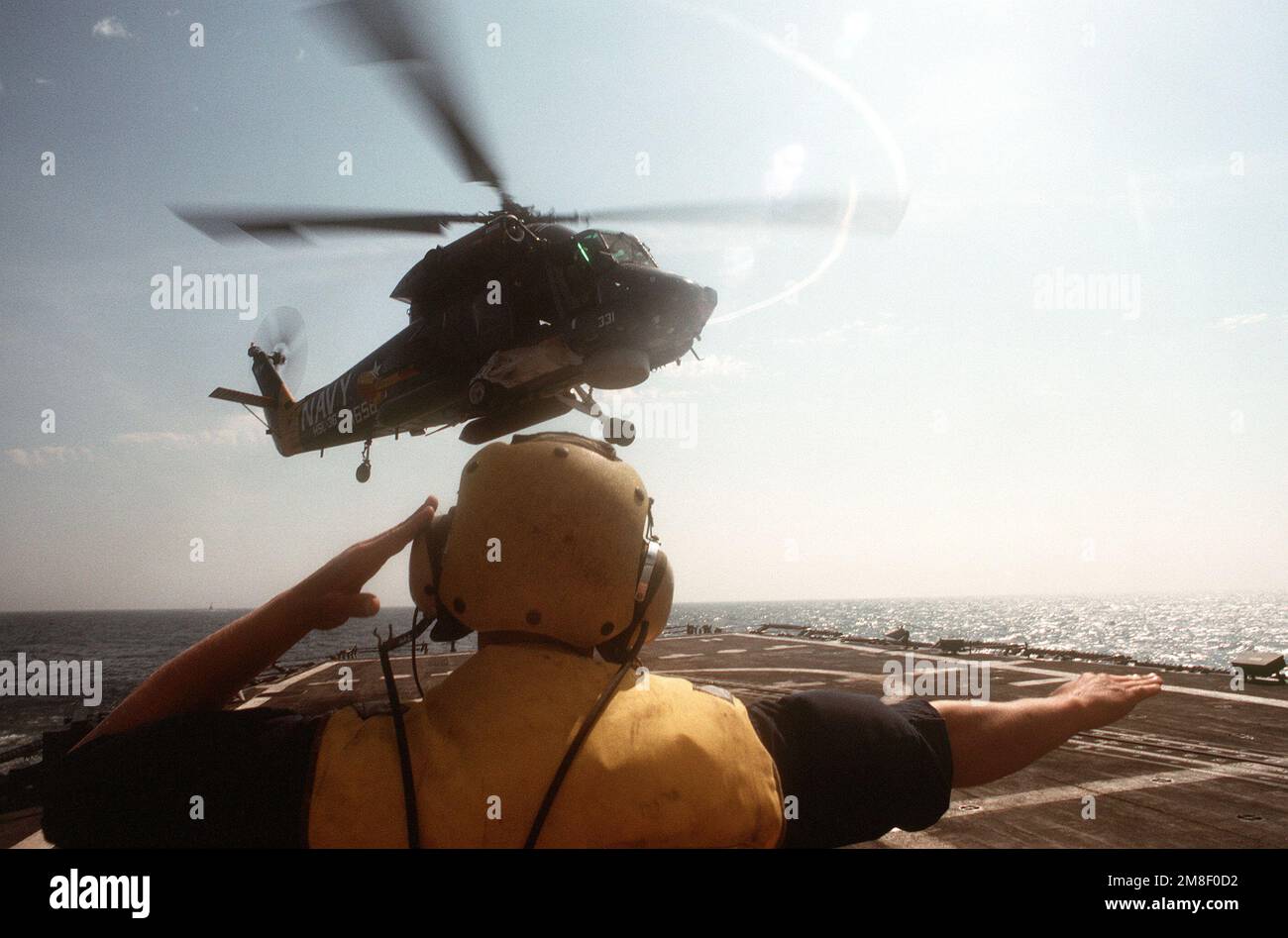 A flight deck crewman signals as a Light Helicopter Anti-submarine ...