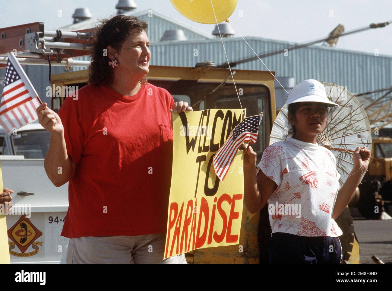 Two women stand on the pier to welcome the guided missile cruiser USS ...