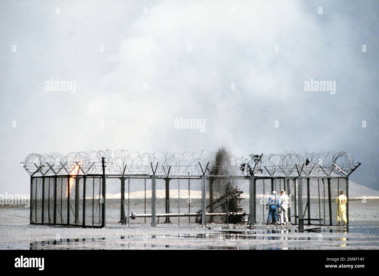 An oil fire burns in the background as firefighters inspect another ...