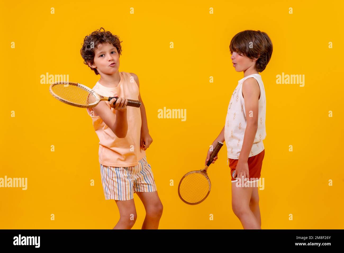 Two kids playing tennis and having fun in summer, yellow background ...