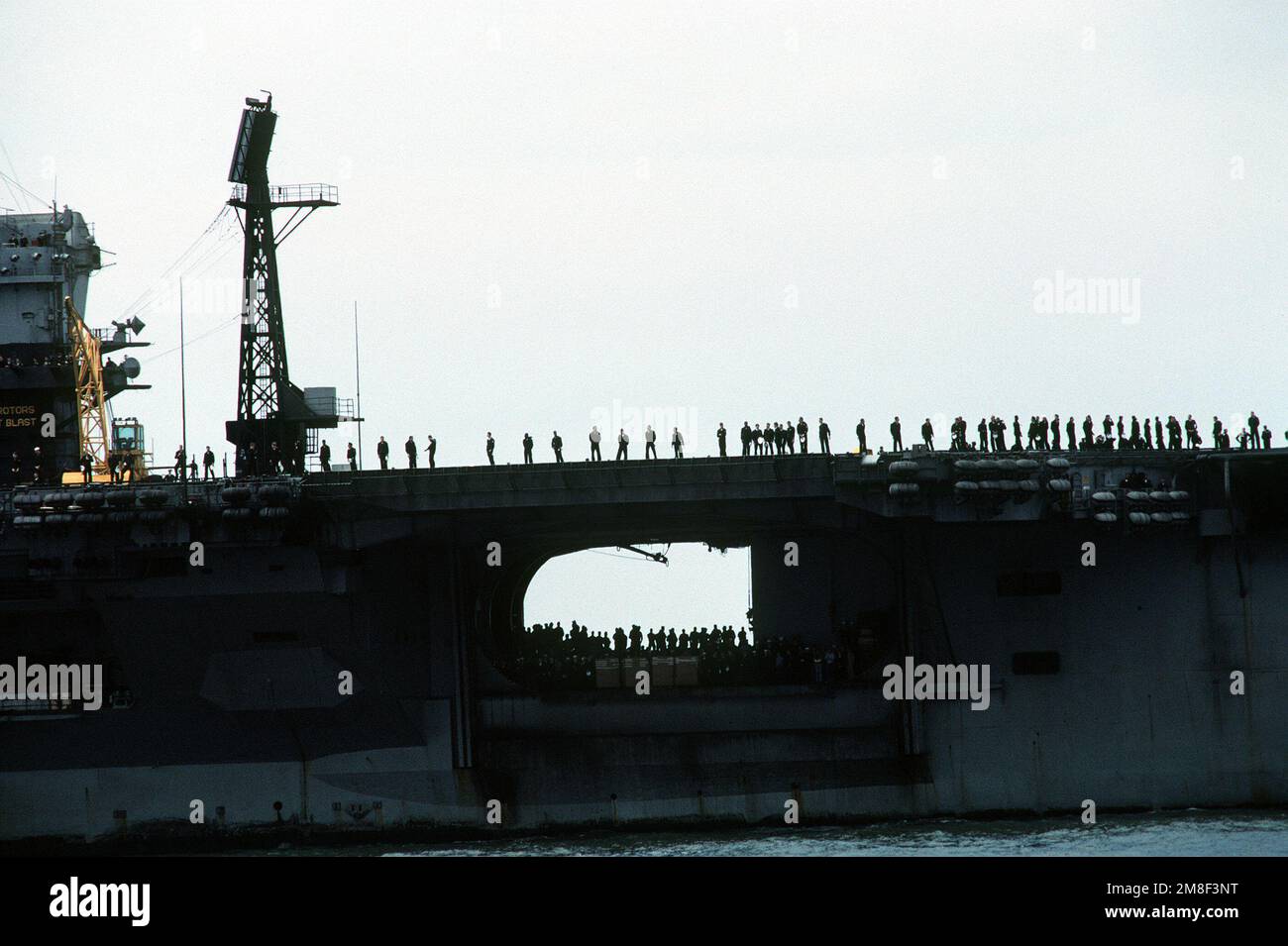 Crew members stand at the railing and in the hangar bay aboard the ...