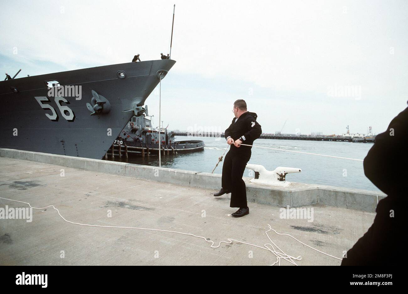 As the large harbor tug MENOMINEE (YTB-790) moves the ship into place ...