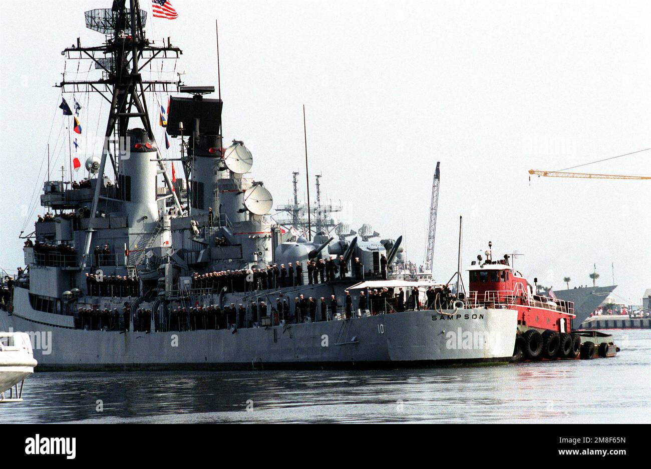 A tug boat pushes the guided missile destroyer USS SAMPSON (DDG-10) into place alongside the ...