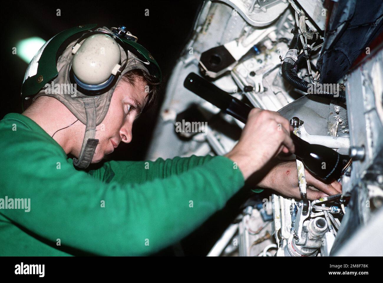 A maintenance crewman uses a flashlight as he inspects an aircraft on ...