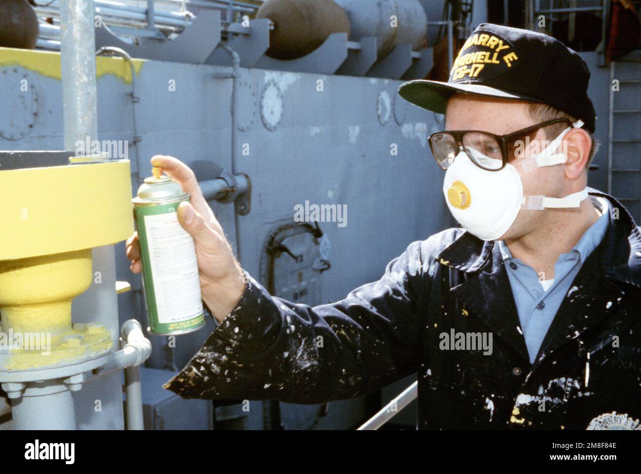 A sailor wears a respirator and safety glasses while spray-painting a ...