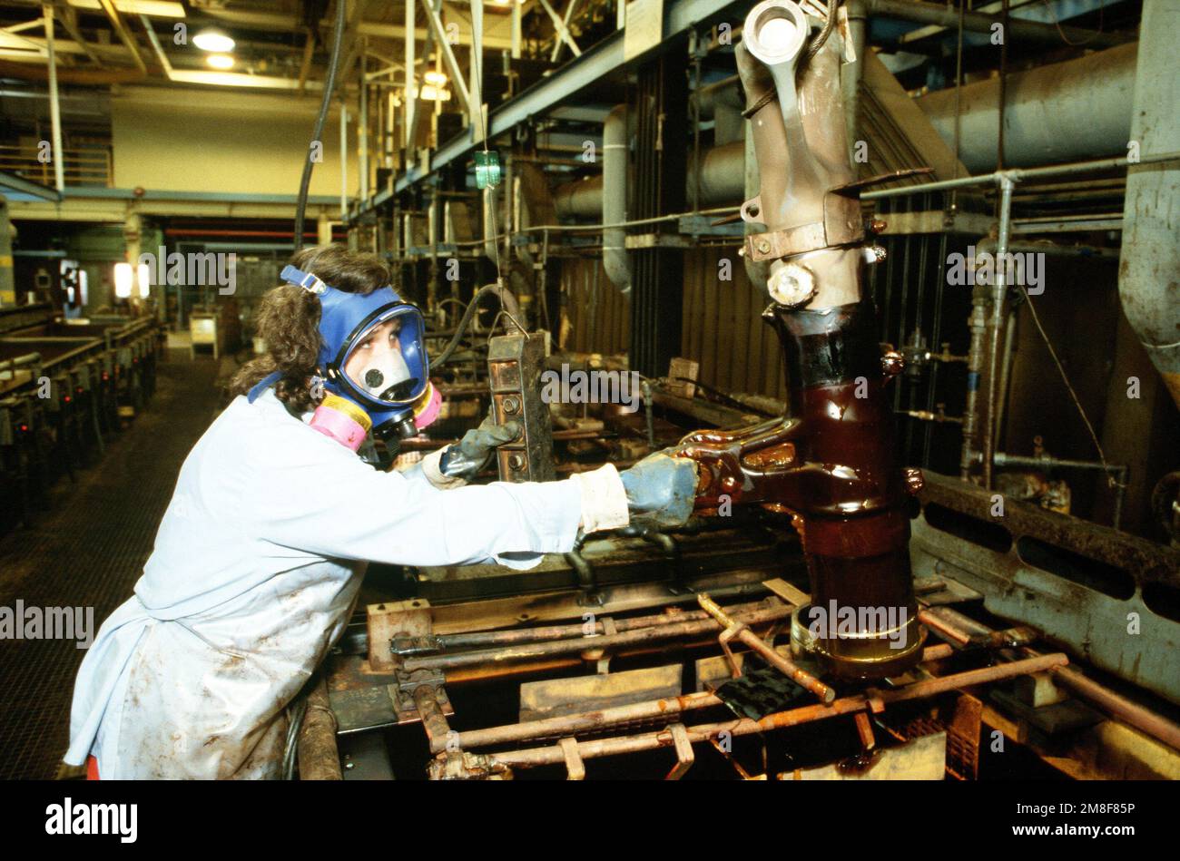 A civilian employee wearing a full-face respirator lifts a fitting from ...