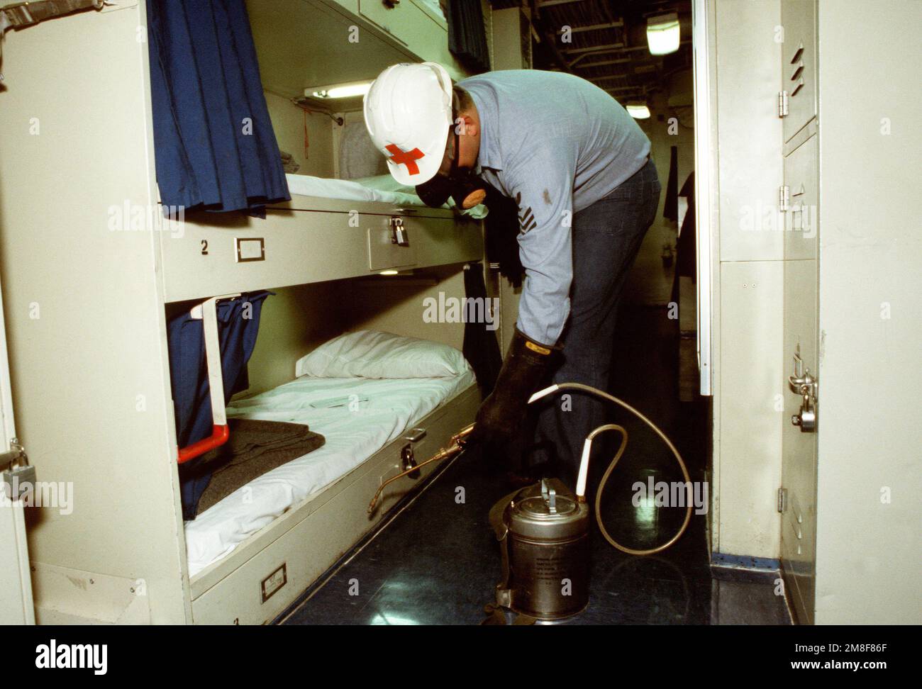 A petty officer wears a goggles and a respirator sprays pesticides in a ...