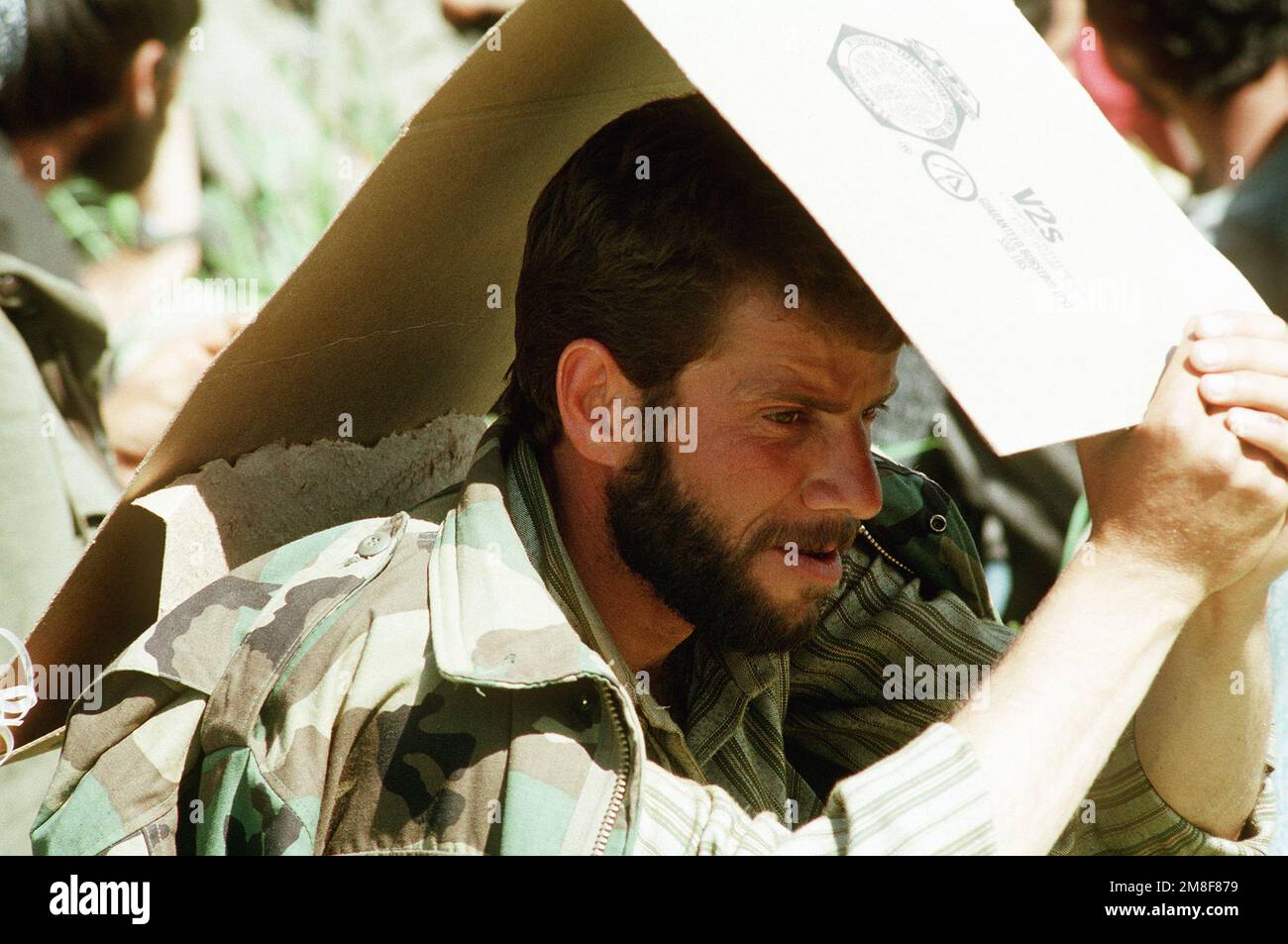 A Kurdish man shades his face with a piece of cardboard as he sits in ...