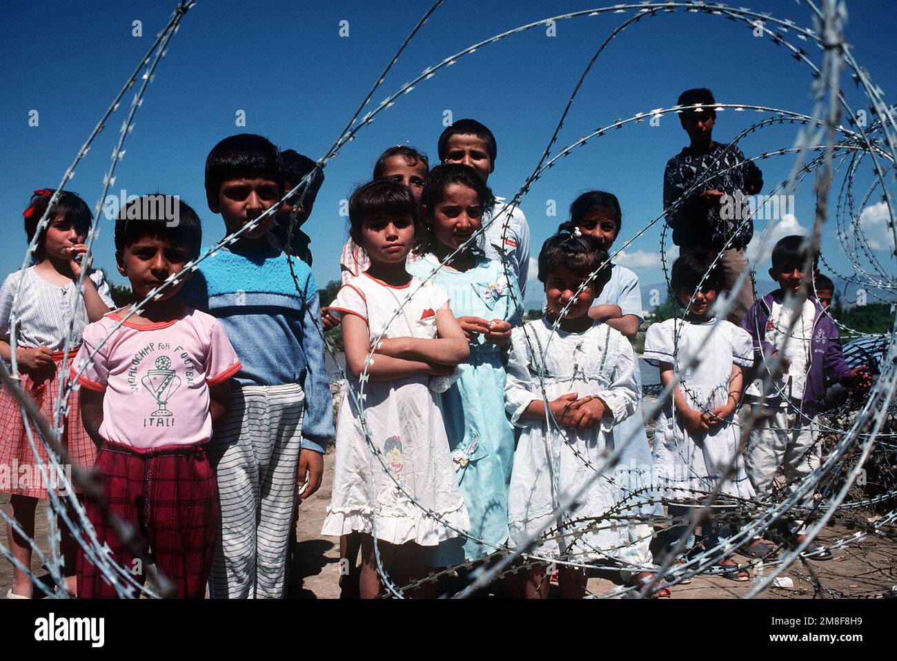 Kurdish children standing behind concertina wire watch as Marines set ...