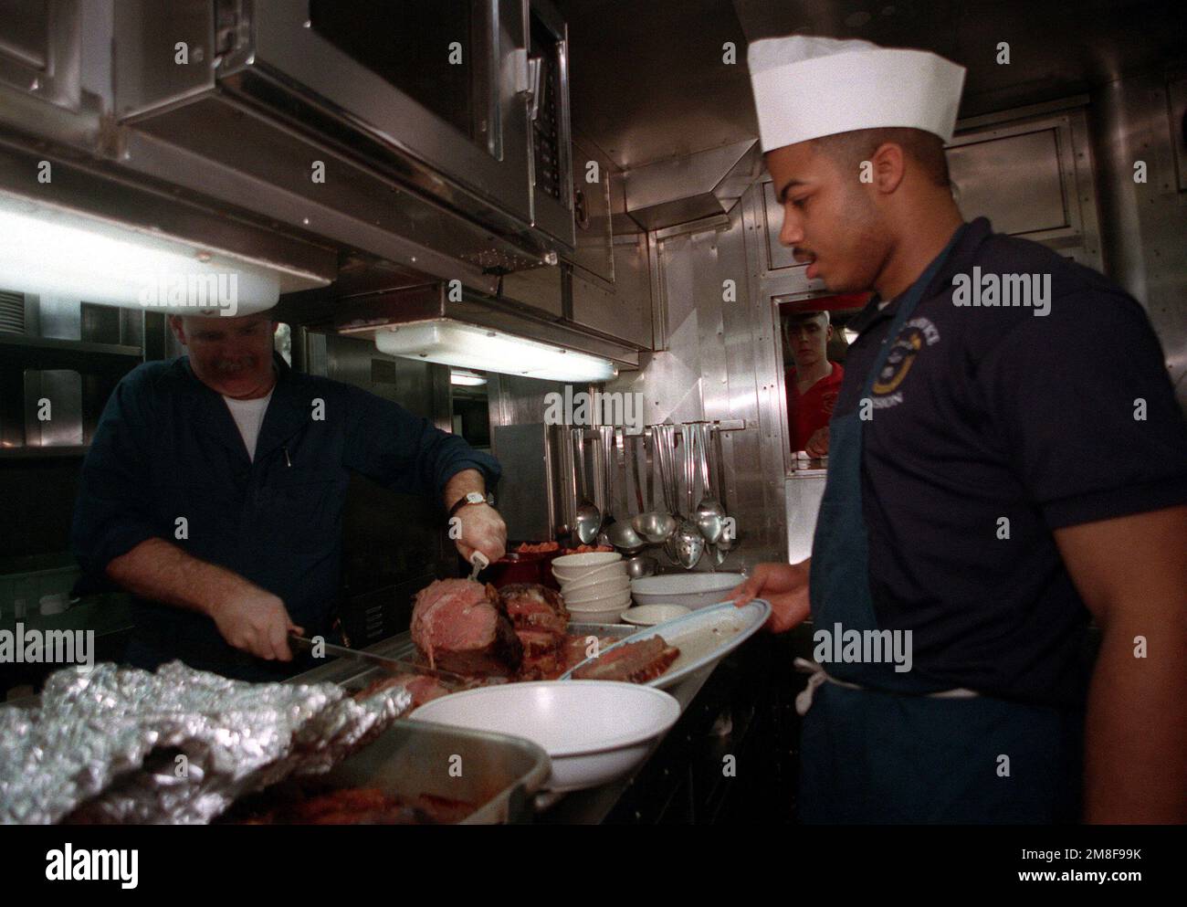Two mess management specialists prepare a platter of meat as dinner is ...