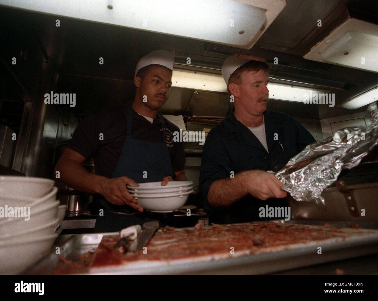 Two mess management specialists prepare to serve dinner aboard the ...