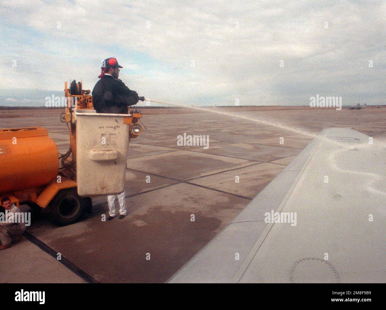 A base worker sprays de-icing solution on the wing of a Fleet Logistic ...