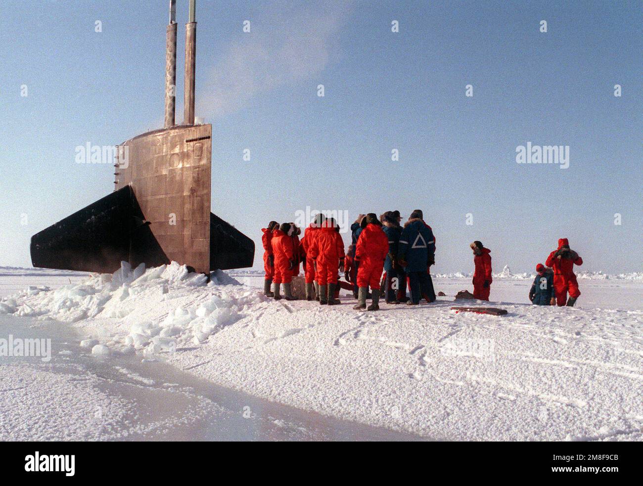 Crewmen and a group of official visitors stand on the ice a top the ...