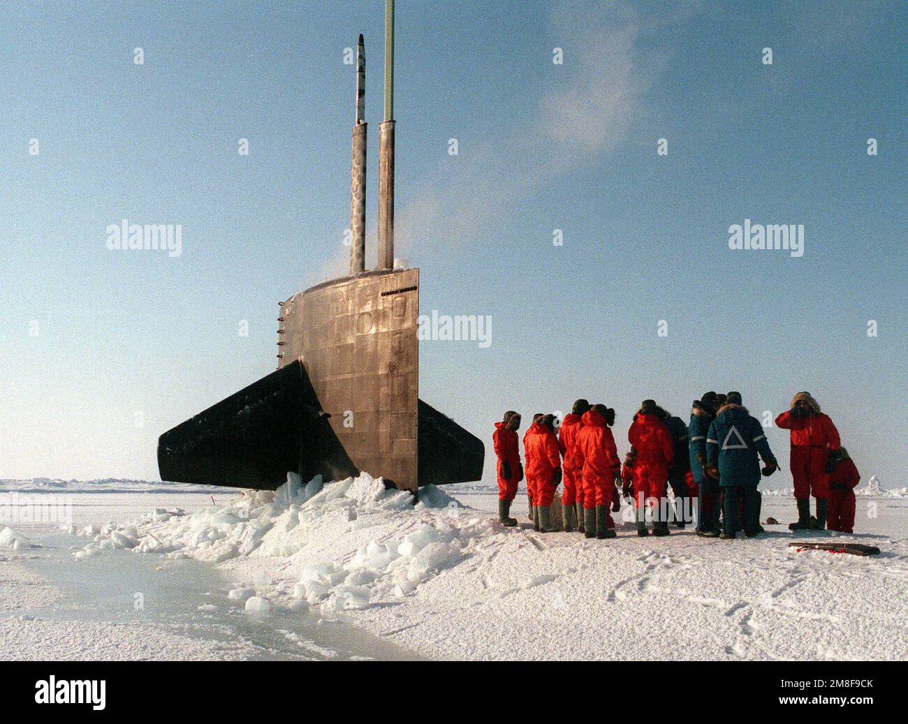 Crewmen and a group of official visitors stand on the ice atop the hull ...
