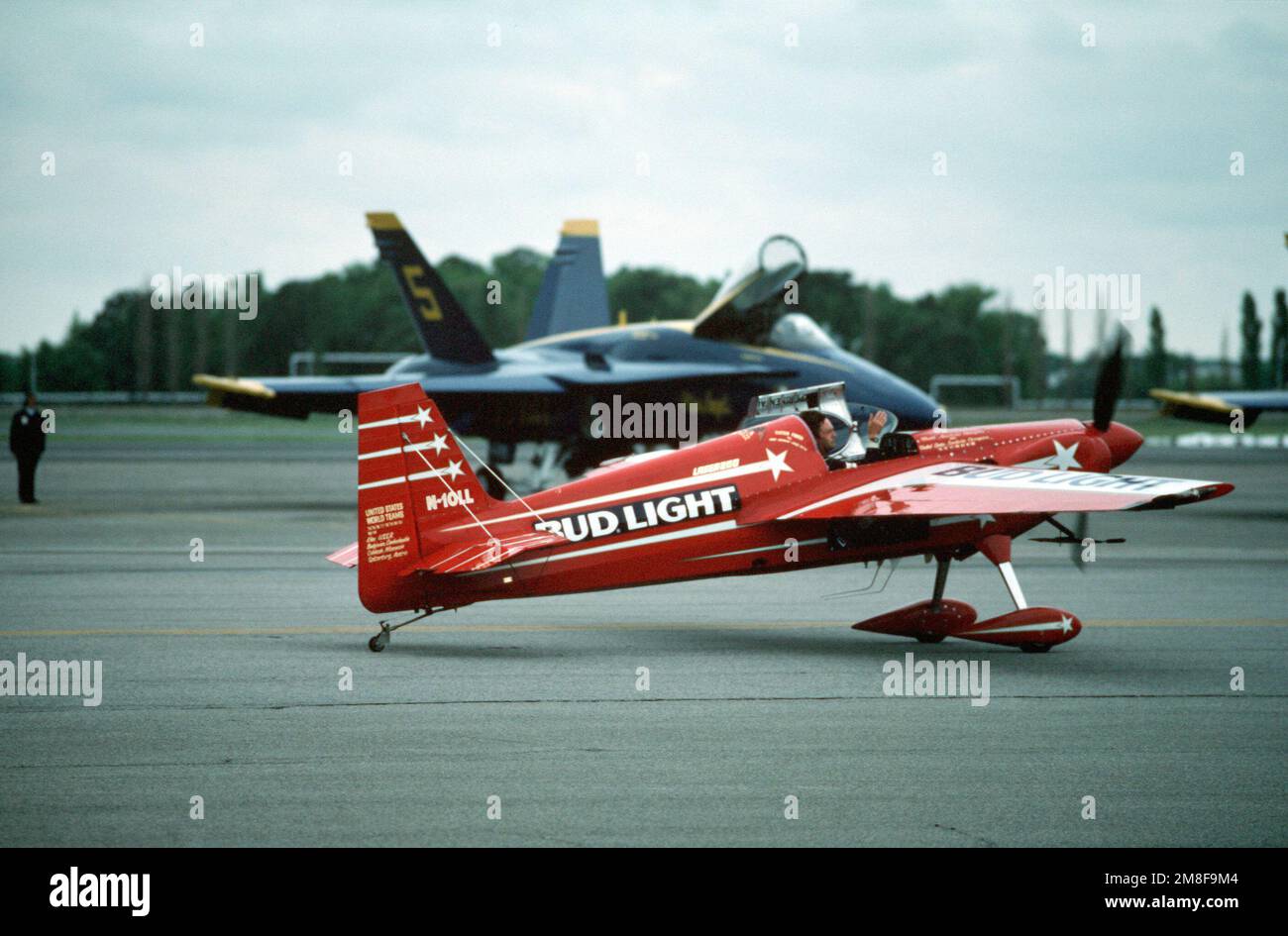 A Laser 200 aerobatic aircraft taxis past an F/A-18A Hornet aircraft of ...