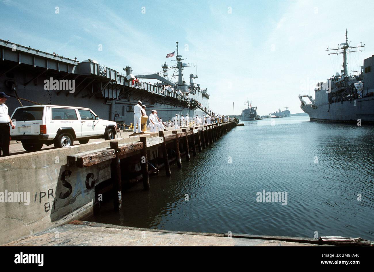 Line handlers stand by on the pier as a large harbor tug pushes a tank ...