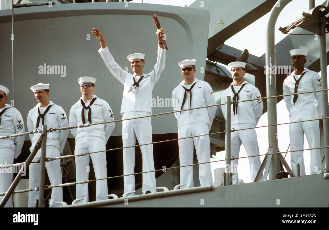 A crew member aboard a tank landing ship waves as he mans the rails ...