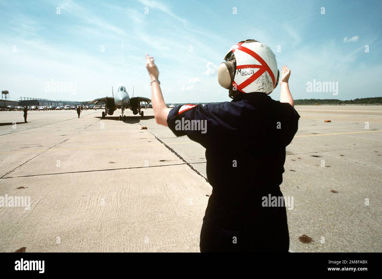 A ground guide signals to the pilot of an F-14A Tomcat aircraft as the ...