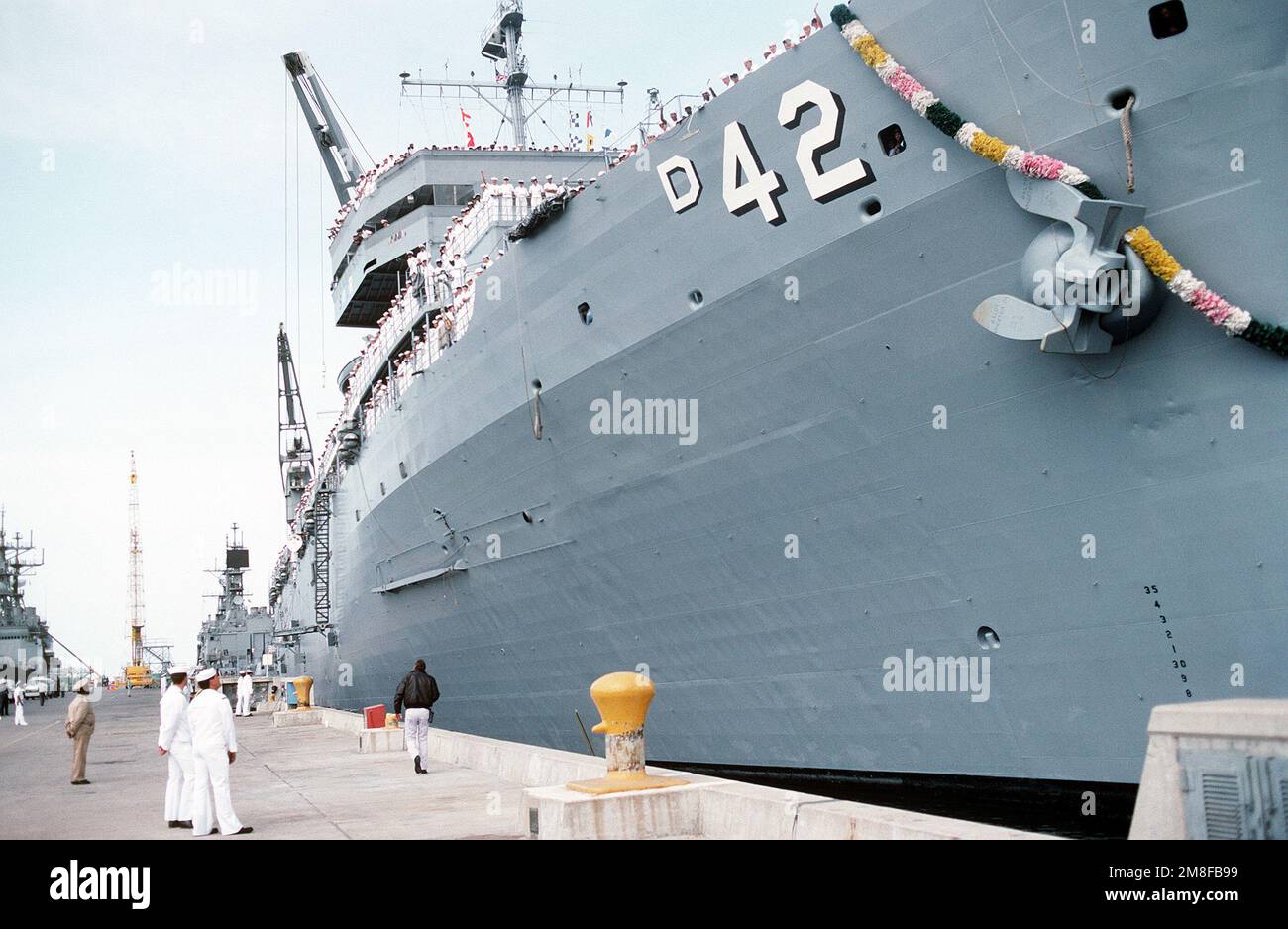 Crew members stand at the railing aboard the destroyer tender USS ...