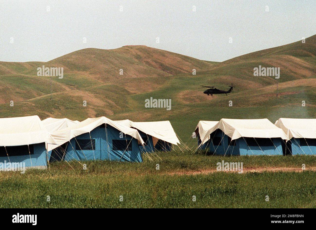 A UH-60 Black Hawk (Blackhawk) helicopter patrols over a tent city near ...