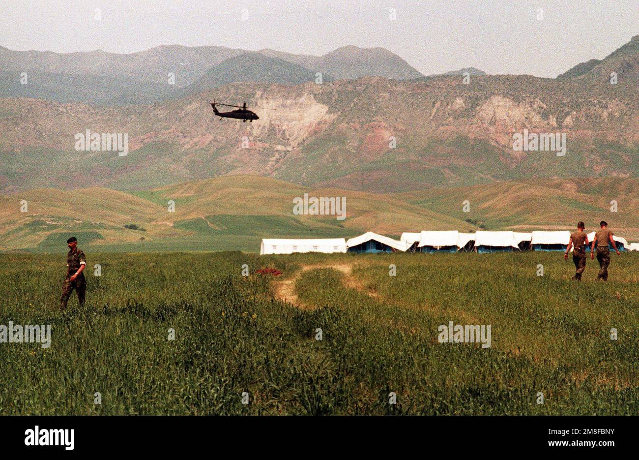 A UH-60 Black Hawk (Blackhawk) helicopter patrols over a tent city near ...