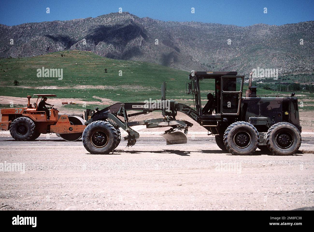 An Army engineer, foreground, drives a motor grader while a Seabee from ...
