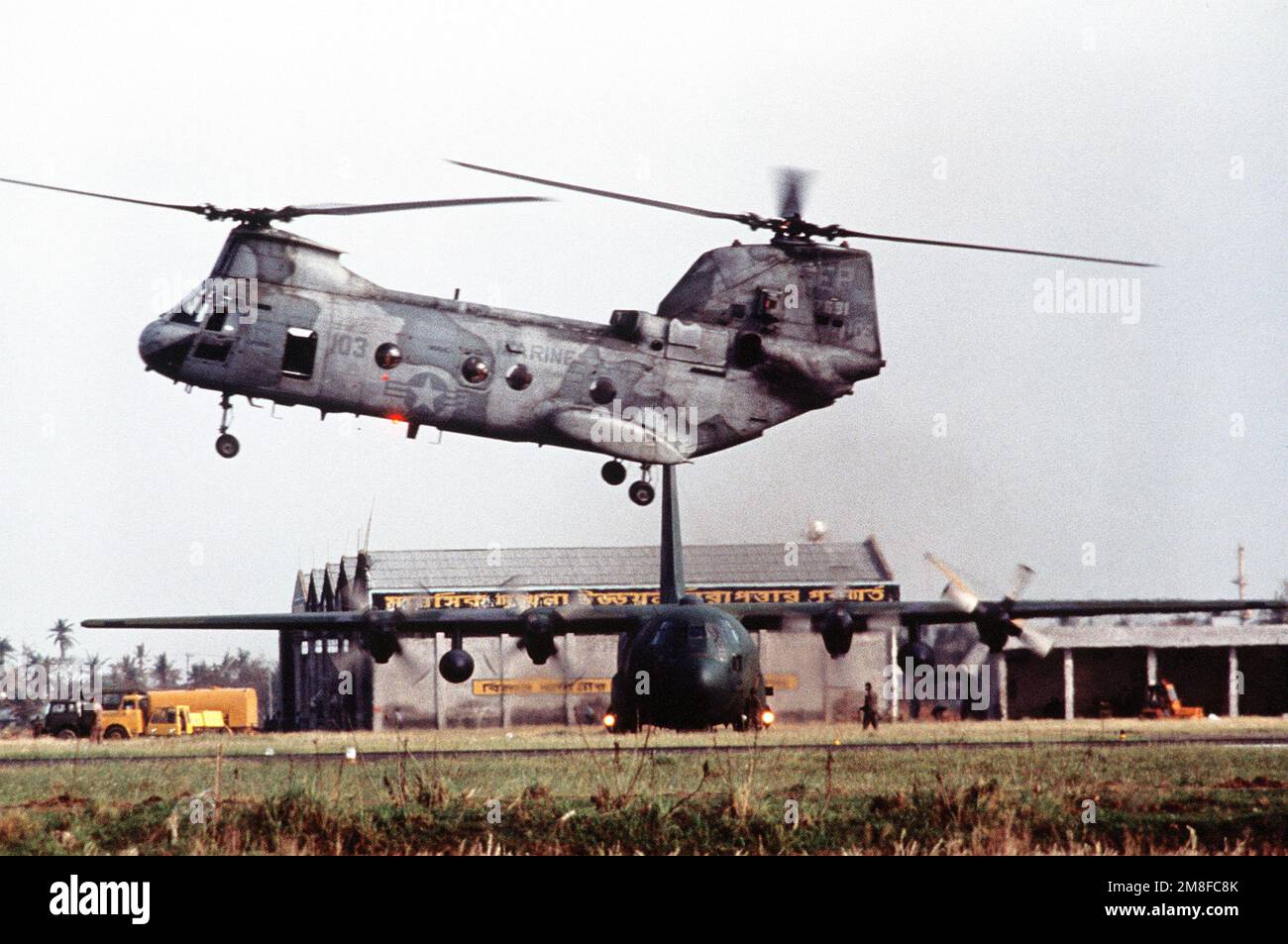 A CH-46 Sea Knight helicopter lands as a 374th Tactical Air Wing C-130 ...
