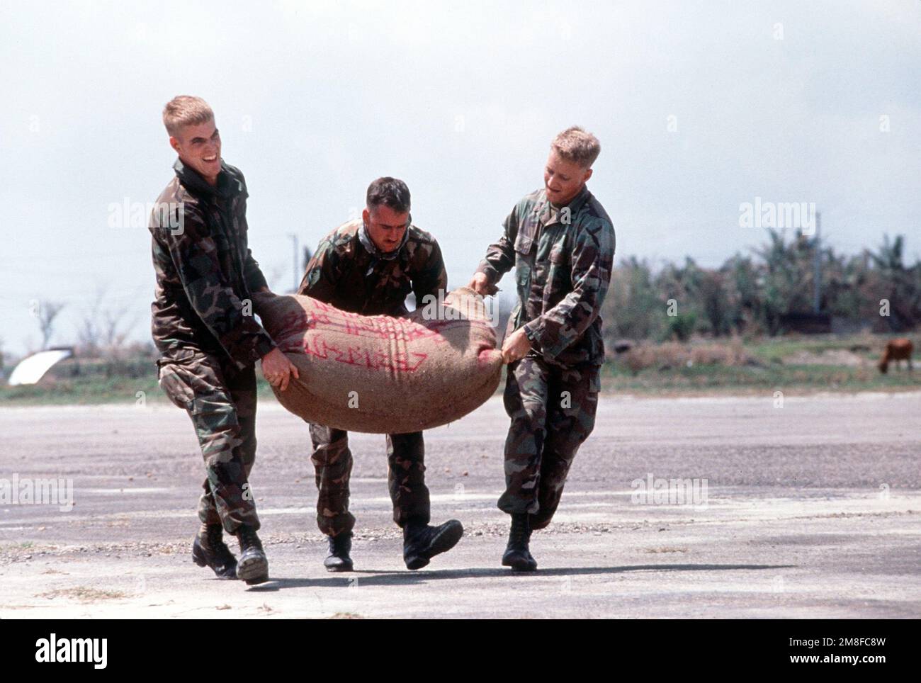 U.S. Marines carry a sack of rice across the airfield at Chittagong Air ...