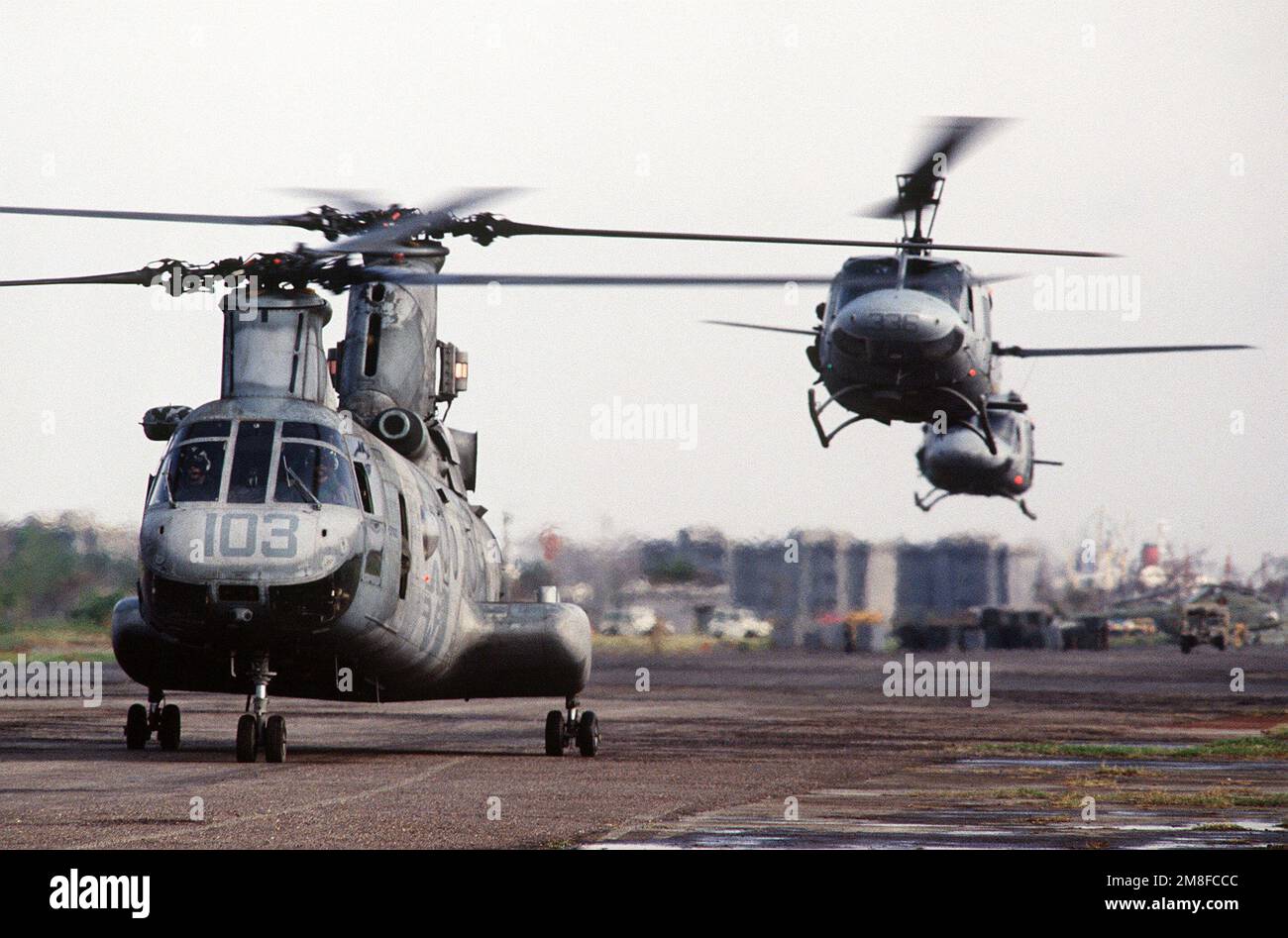 UH-1 Iroquois helicopters hover above the airfield as a CH-46 Sea ...