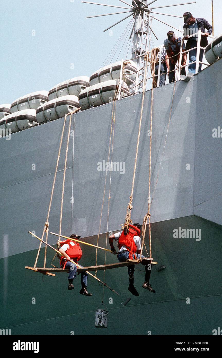 Crew members paint the hull of the amphibious command ship USS BLUE ...