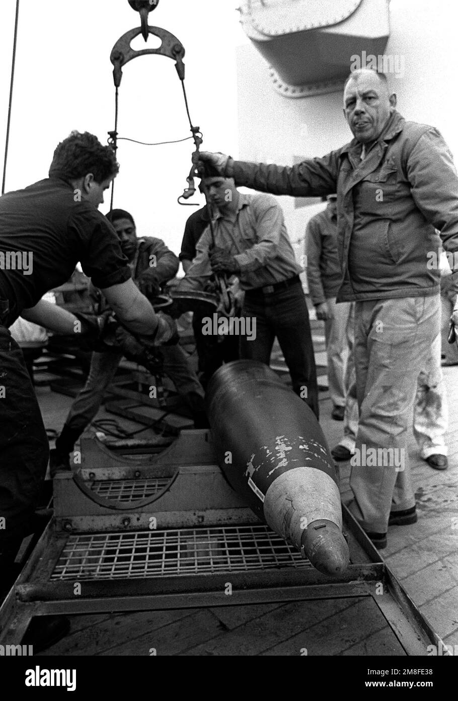 Crewmen secure a hoist used to lower a 16-inch projectile to a pallet ...