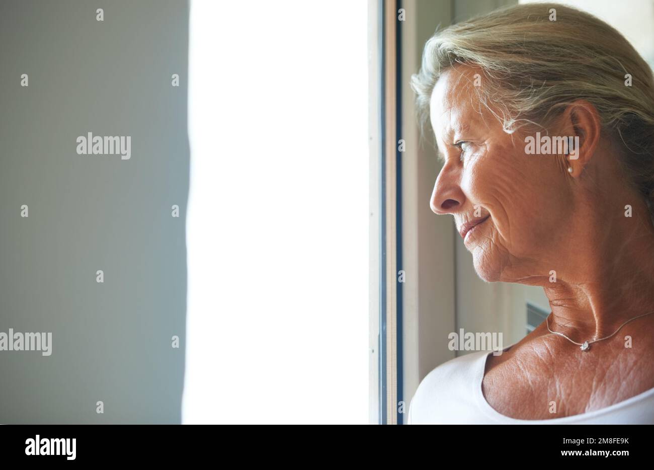 Contemplating her retirement years. Elderly woman looking out a window ...