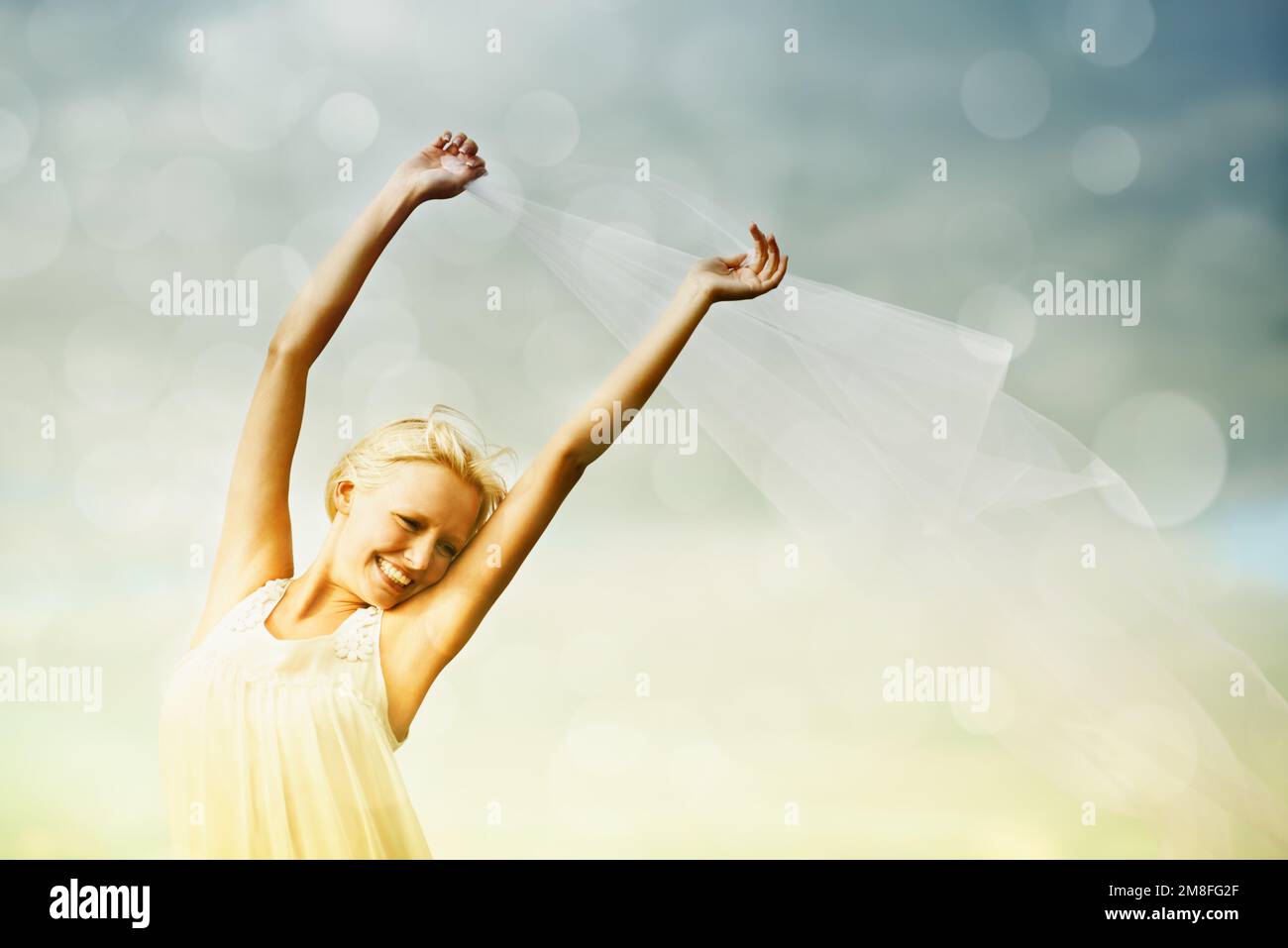 With the wind in her hair. A young woman holding chiffon blowing in the wind surrounded by bokeh ...