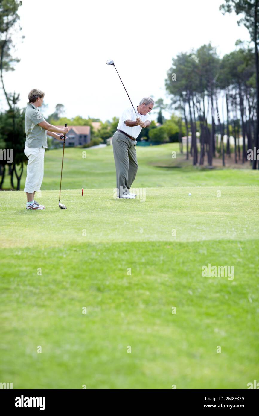 Focus and precision in every shot. A senior male swinging his driver ...