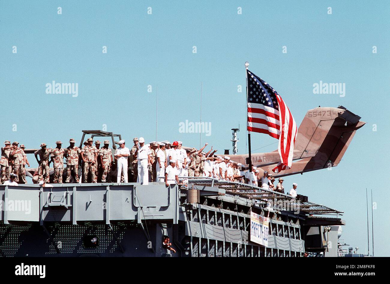 Sailors and Marines stand near the colors at the stern of the ...