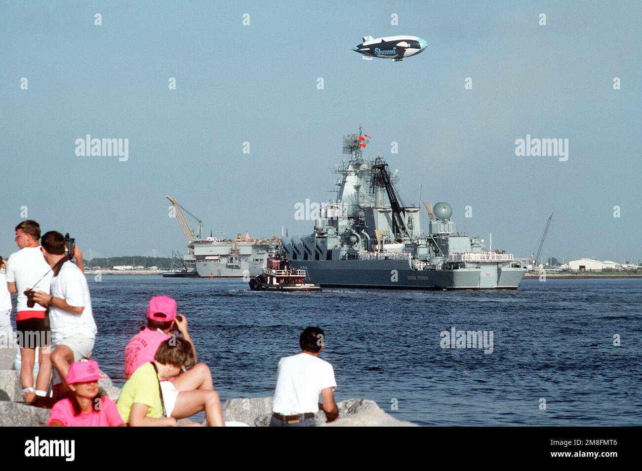 The airship Shamu passes overhead as a tug boat escorts the Soviet ...