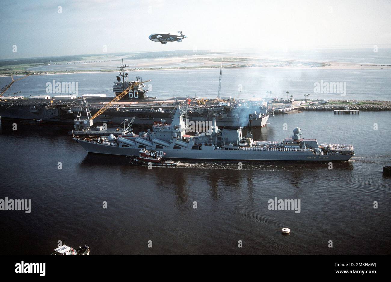 The Sea World airship travels overhead as a large harbor tug escorts ...