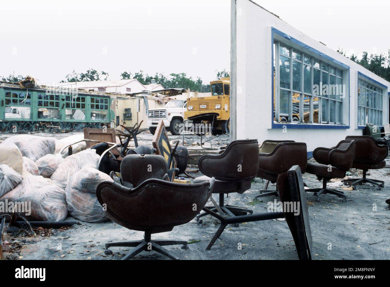 Ruined chairs and bags of trash sit near a wall as workers clear debris ...
