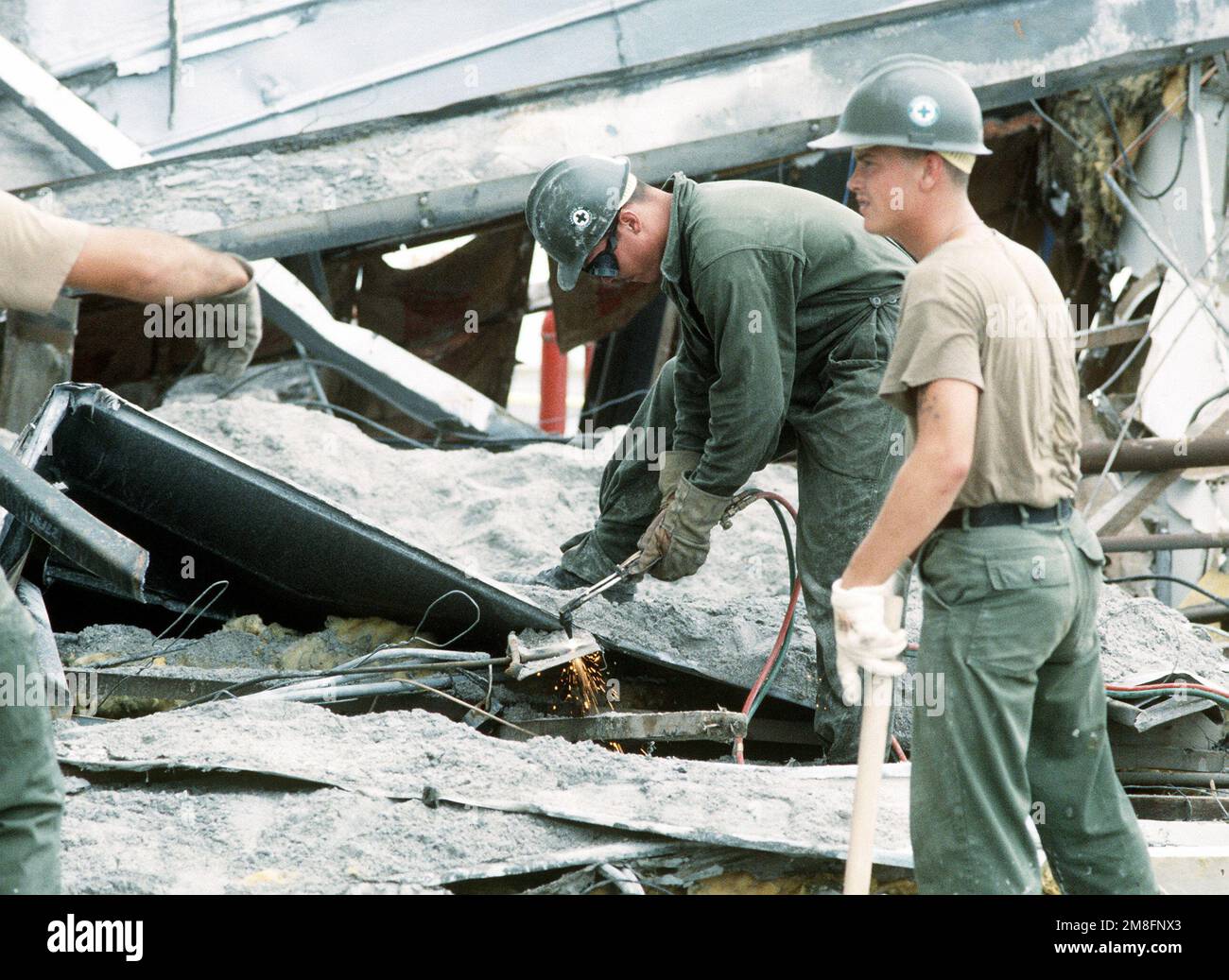A Seabee uses a cutting torch to separte some of the metal debris in a ...